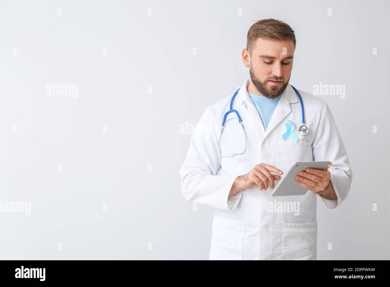 Doctor with blue ribbon and tablet computer on light background ...