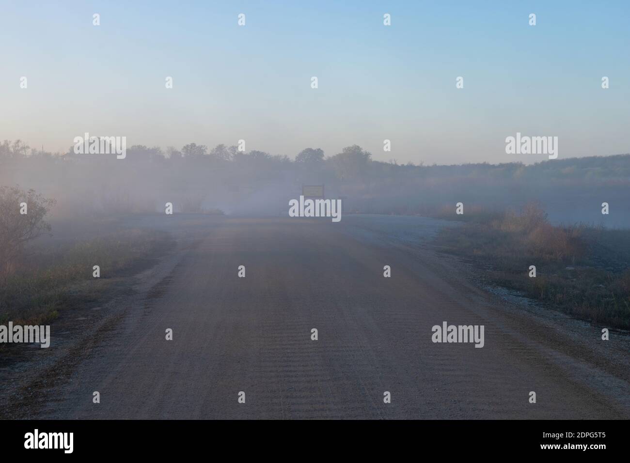 Fog rolling across a dirt road by a lake as the sun rises on a cool ...