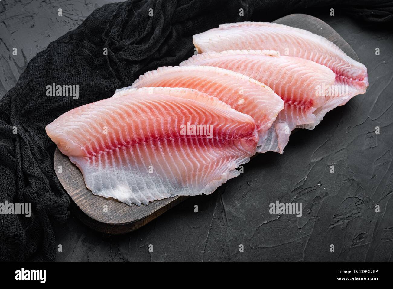 Raw tilapia fish fillet meat cuts, on black background Stock Photo - Alamy