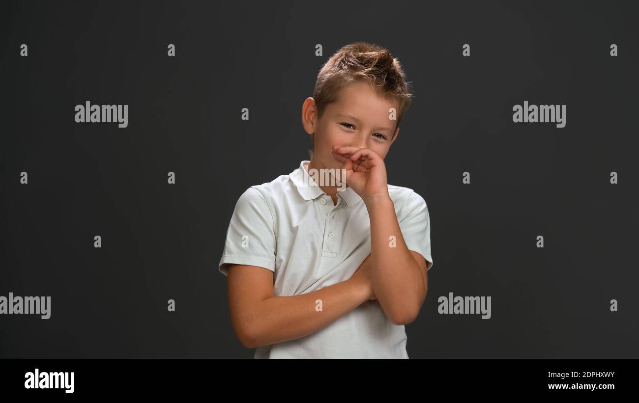 Shyly laughing boy covers his face with his hand looking at the camera ...