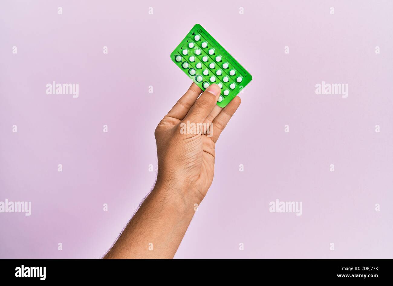 Young hispanic hand holding birth control pills over isolated pink ...