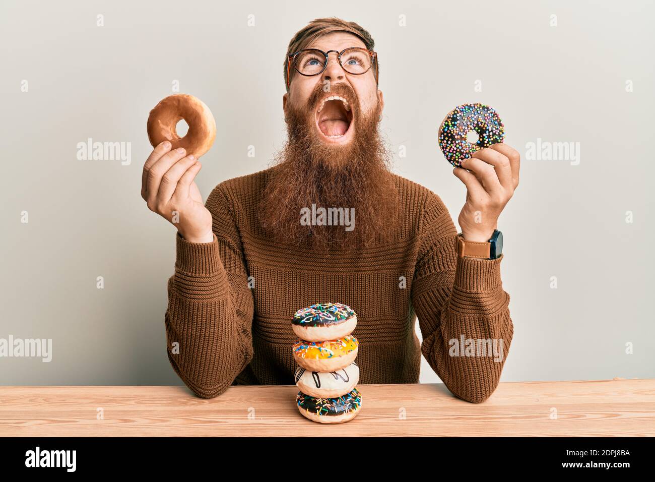 Young irish redhead man eating doughnut for breakfast angry and mad ...