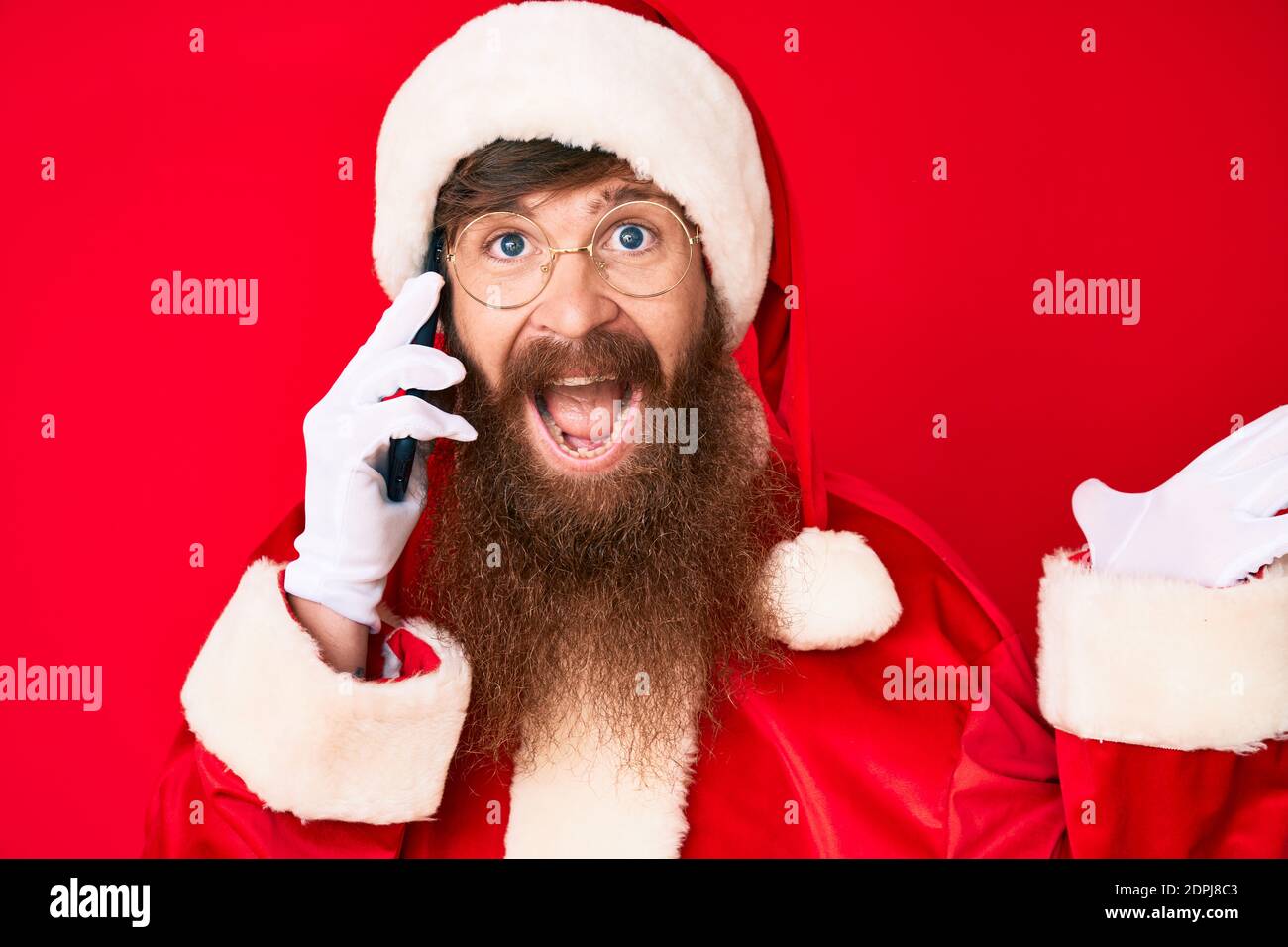 Handsome young red head man with long beard wearing santa claus costume ...