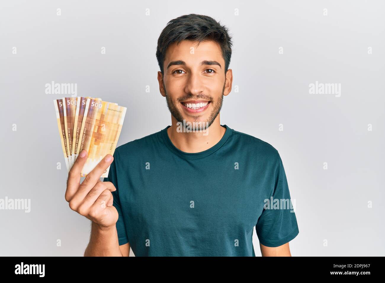 Young handsome man holding 500 norwegian krone banknotes looking ...