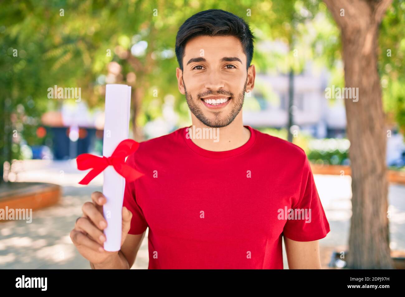 Young latin man smiling happy holding graduated diploma standing at the ...