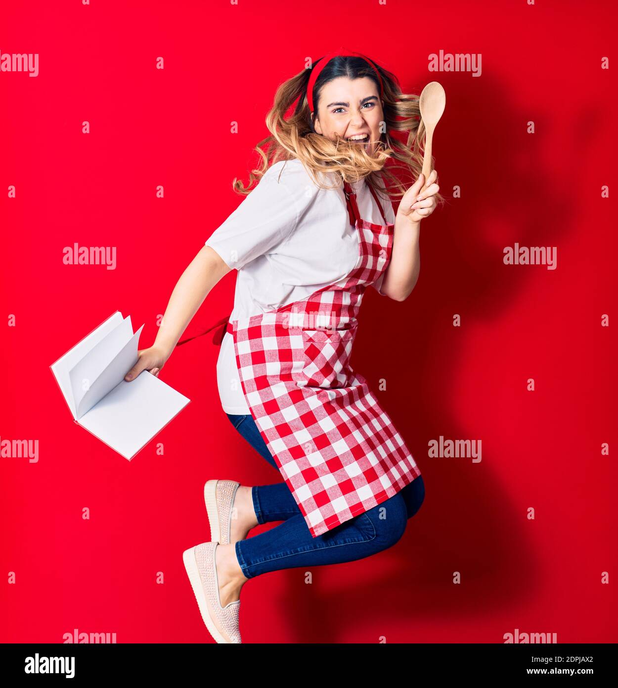 Young beautiful blonde cook woman wearing apron smiling happy. Jumping ...