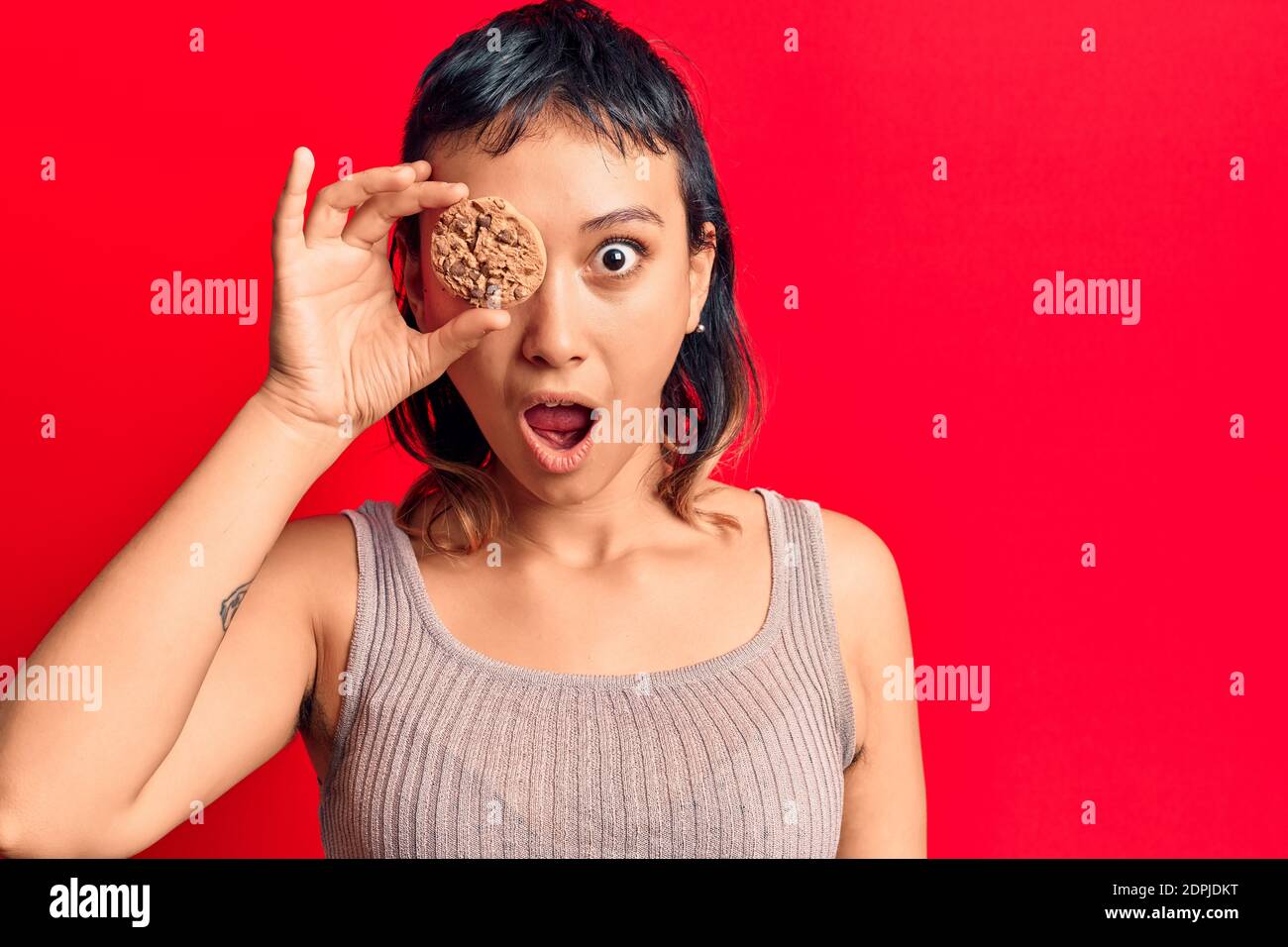 Young woman holding cookie scared and amazed with open mouth for ...