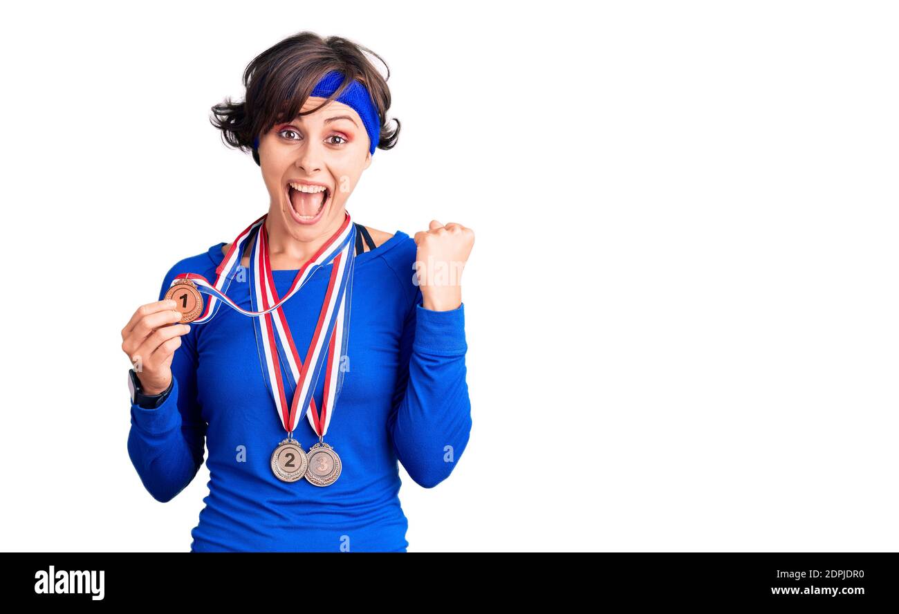 Beautiful young woman with short hair wearing winner medals screaming ...