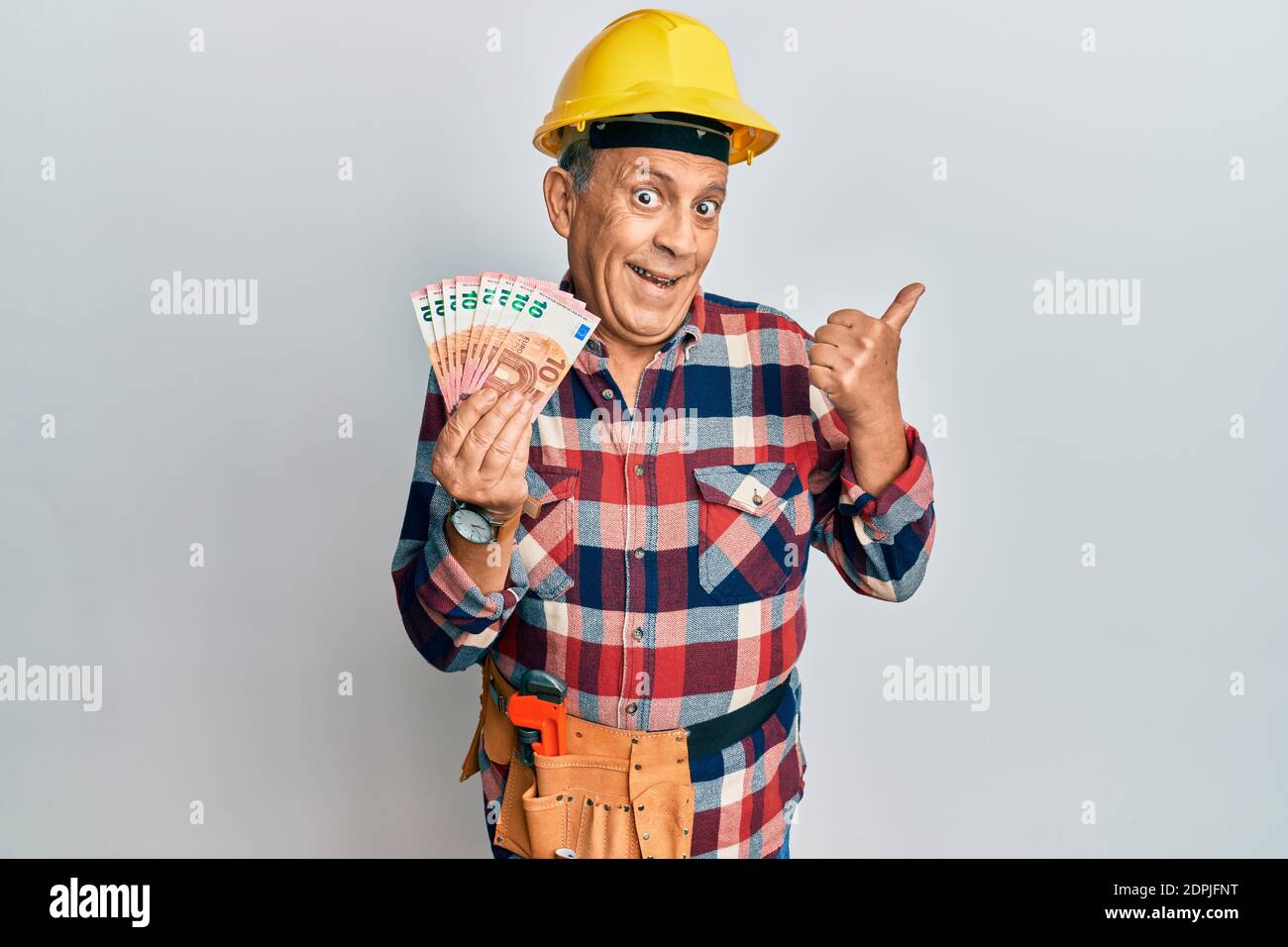 Senior hispanic man wearing handyman uniform and hardhat pointing thumb ...