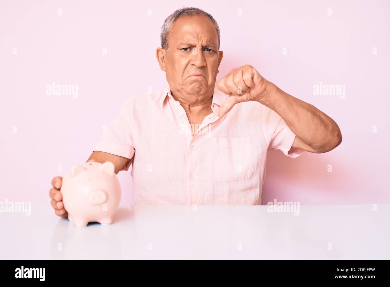 Senior handsome man with gray hair holding piggy bank sitting on the ...
