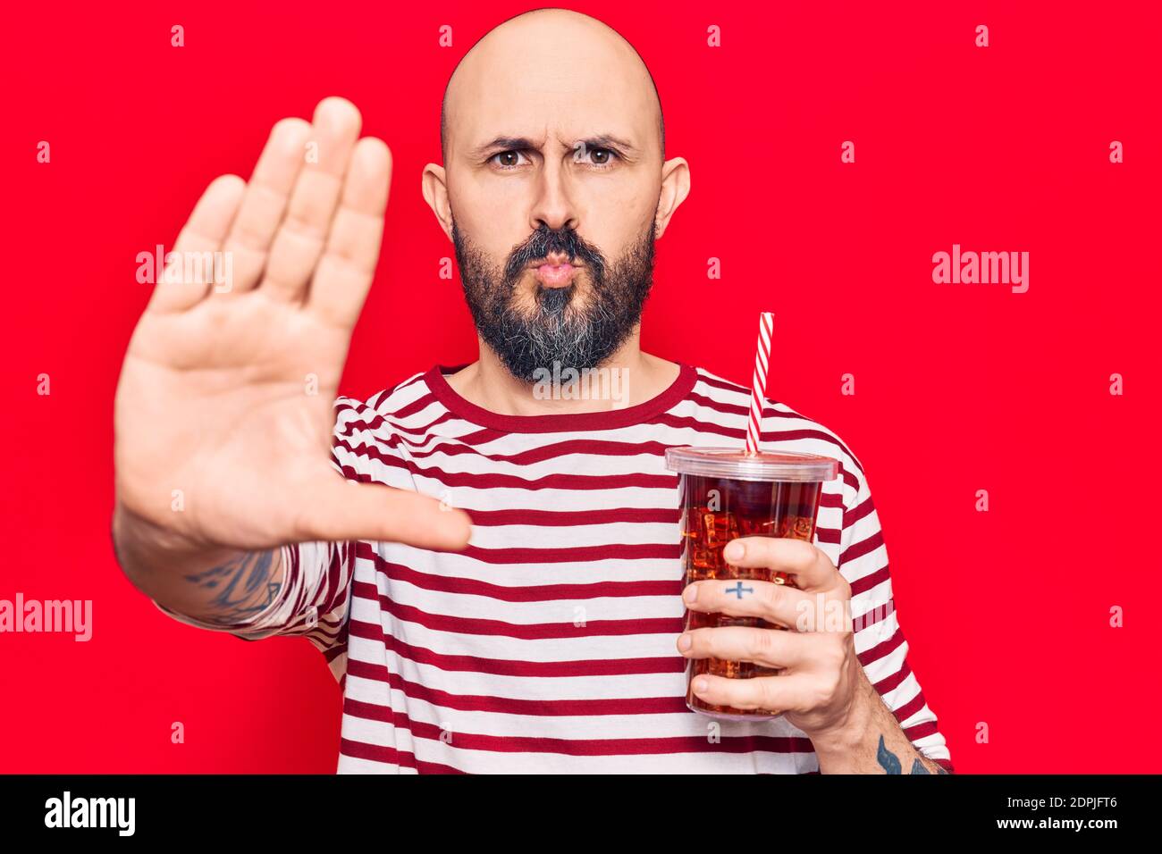 Young handsome man drinking glass of cola beverage with open hand doing ...