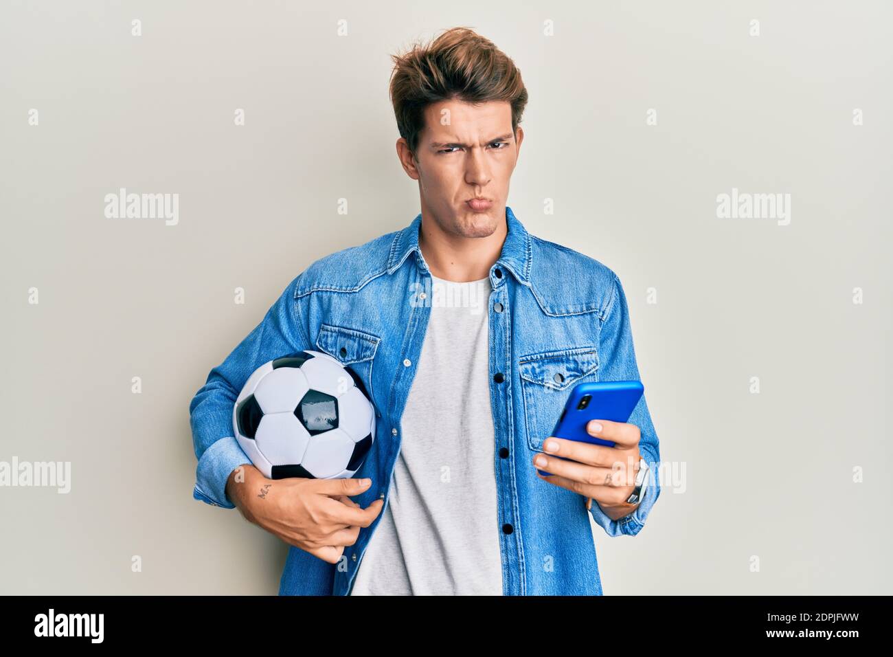 Handsome caucasian man holding football ball looking at smartphone ...