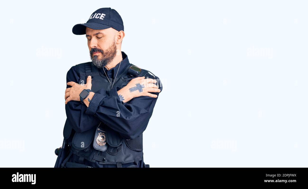 Young handsome man wearing police uniform hugging oneself happy and ...