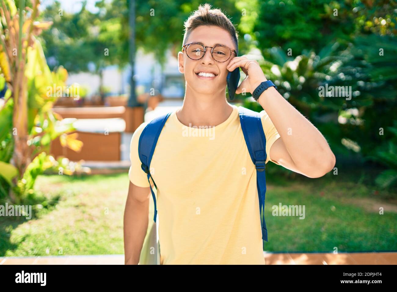 Young hispanic student smiling happy using smartphone walking the ...