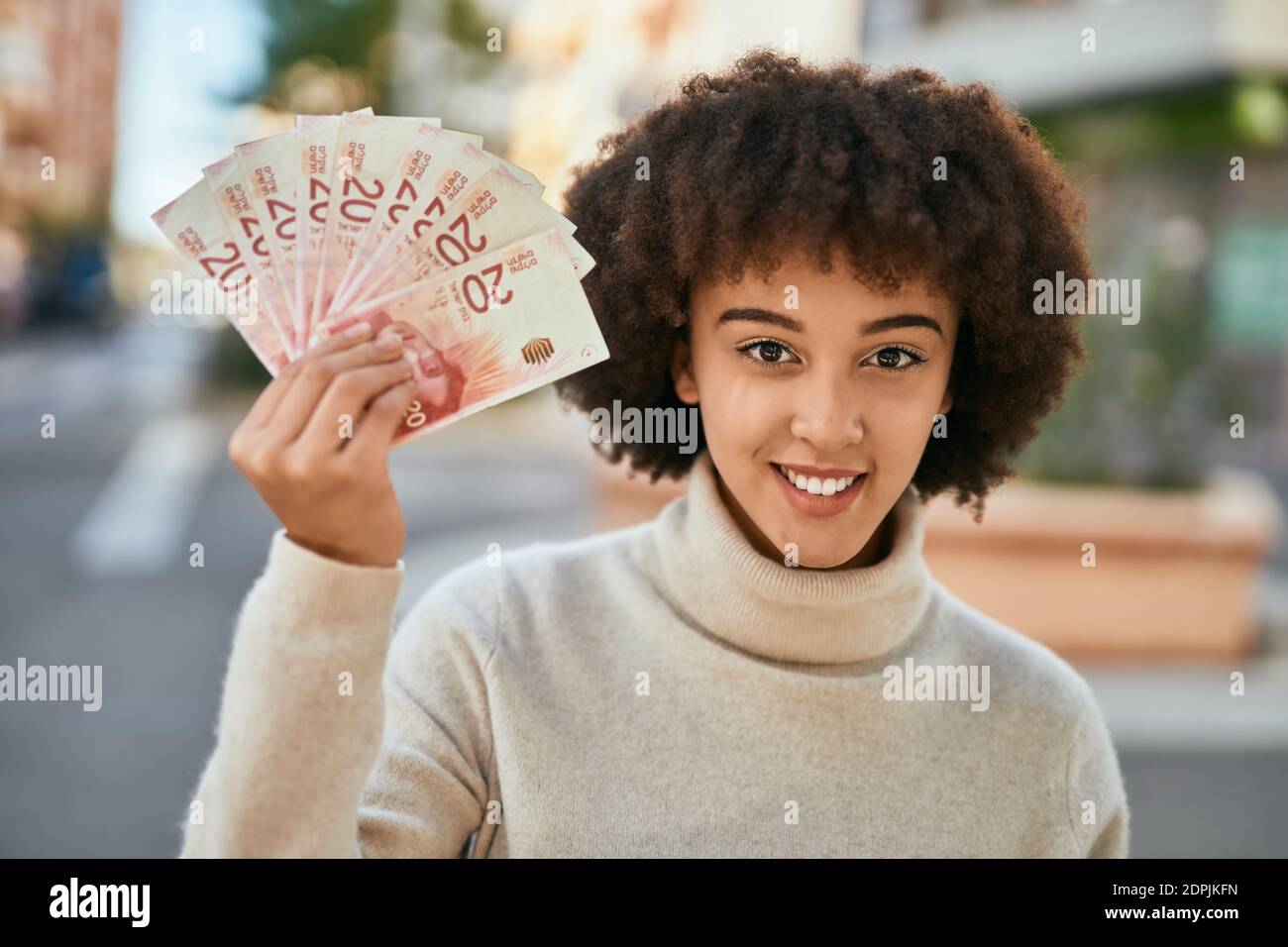 Young hispanic girl smiling happy holding israel shekels at the city ...