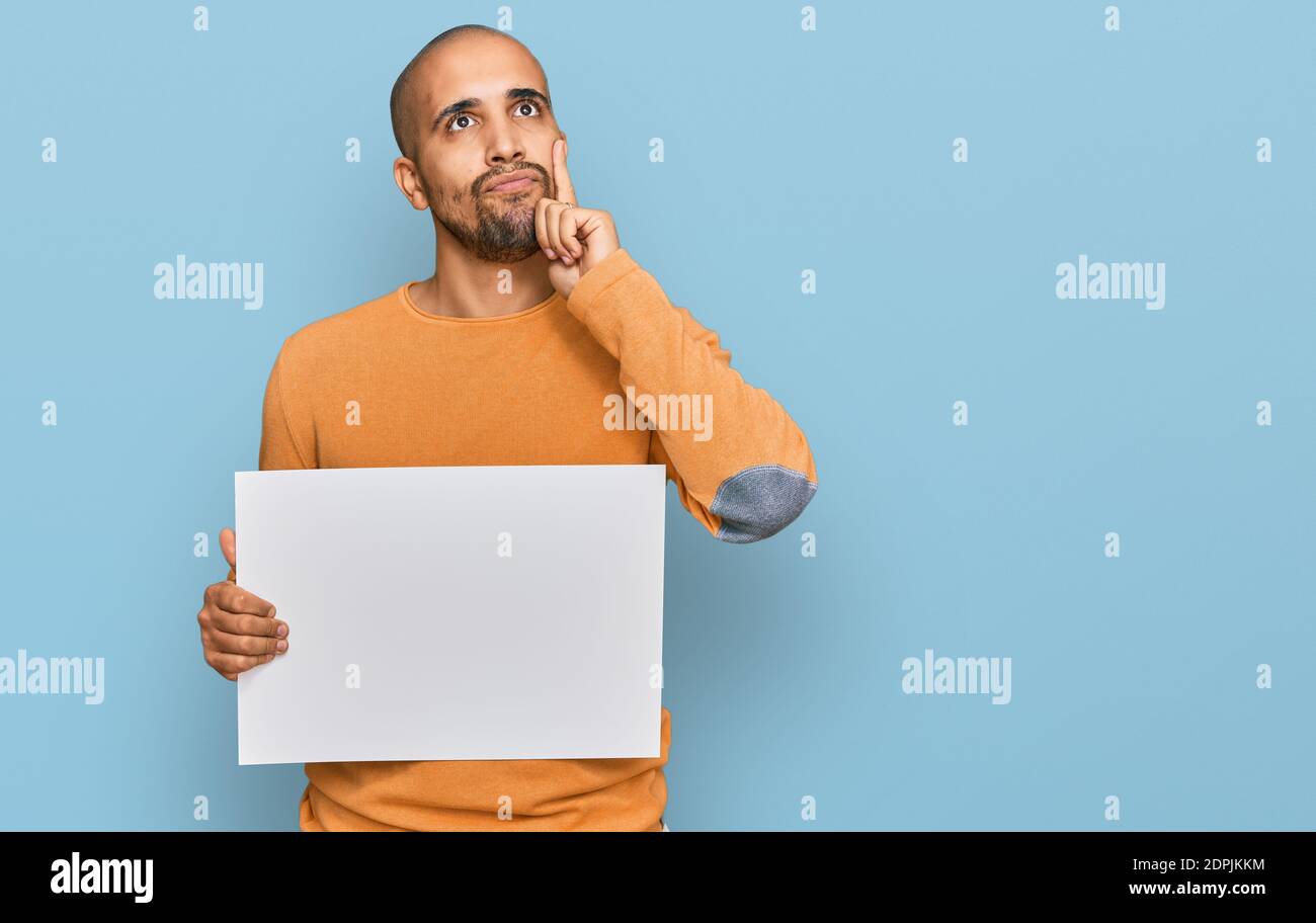 Hispanic adult man holding blank empty banner serious face thinking ...