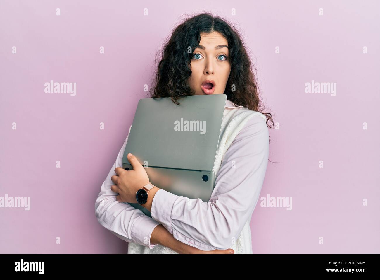Young brunette woman with curly hair hugging laptop with love afraid ...