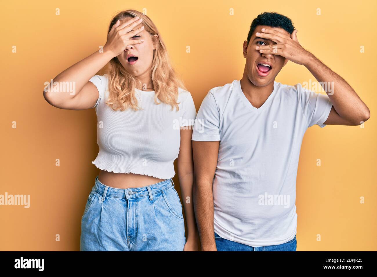 Young interracial couple wearing casual white tshirt peeking in shock ...