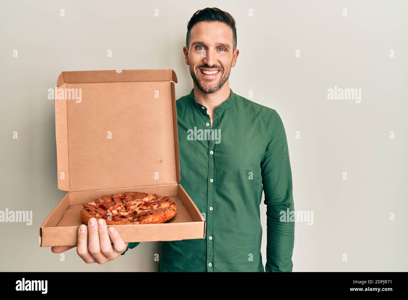 Handsome man with beard holding italian pizza looking positive and ...