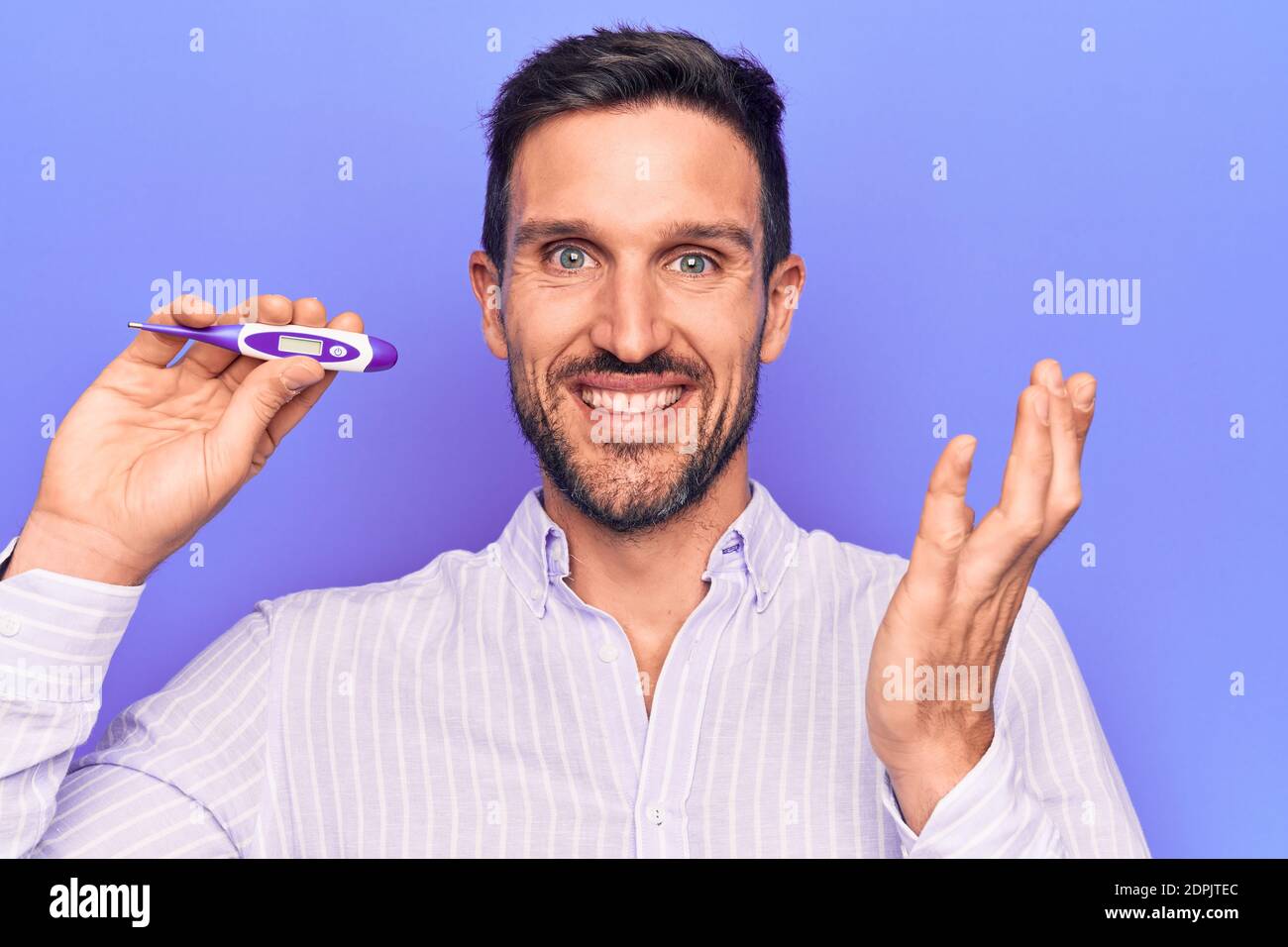 Young handsome man controlling temperature holding thermometer over ...