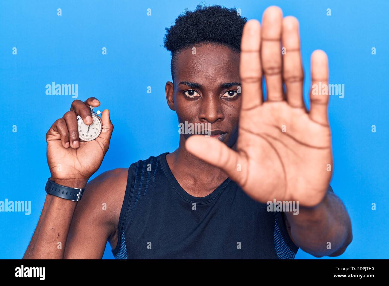 Young african american man holding stopwatch with open hand doing stop ...