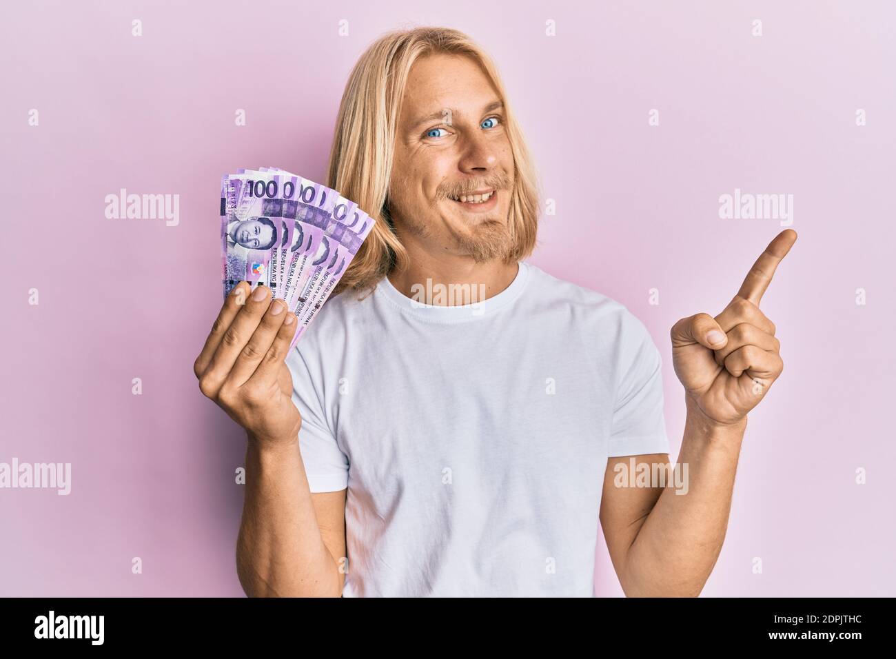 Caucasian young man with long hair holding 100 philippine peso ...