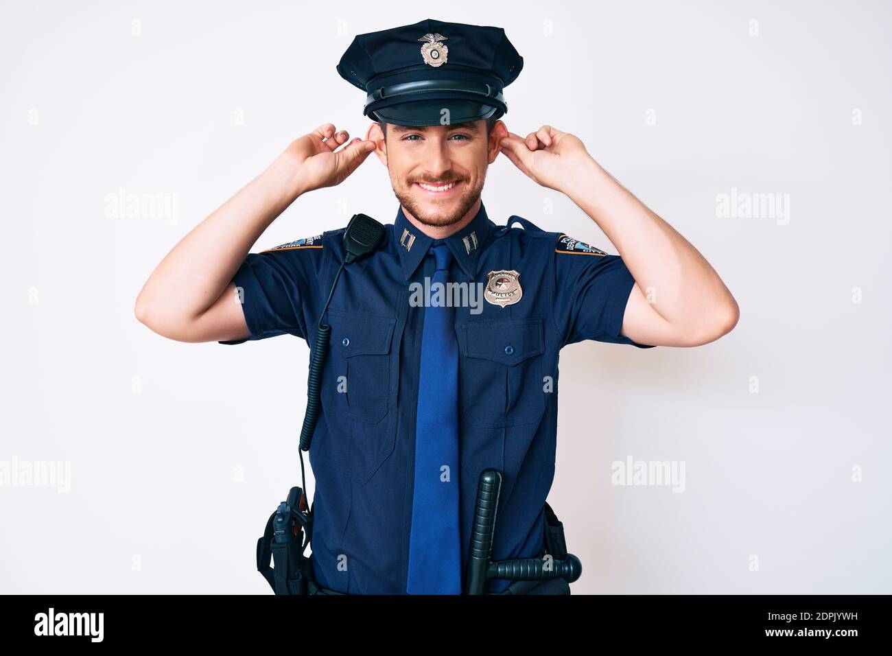 Young caucasian man wearing police uniform smiling pulling ears with ...