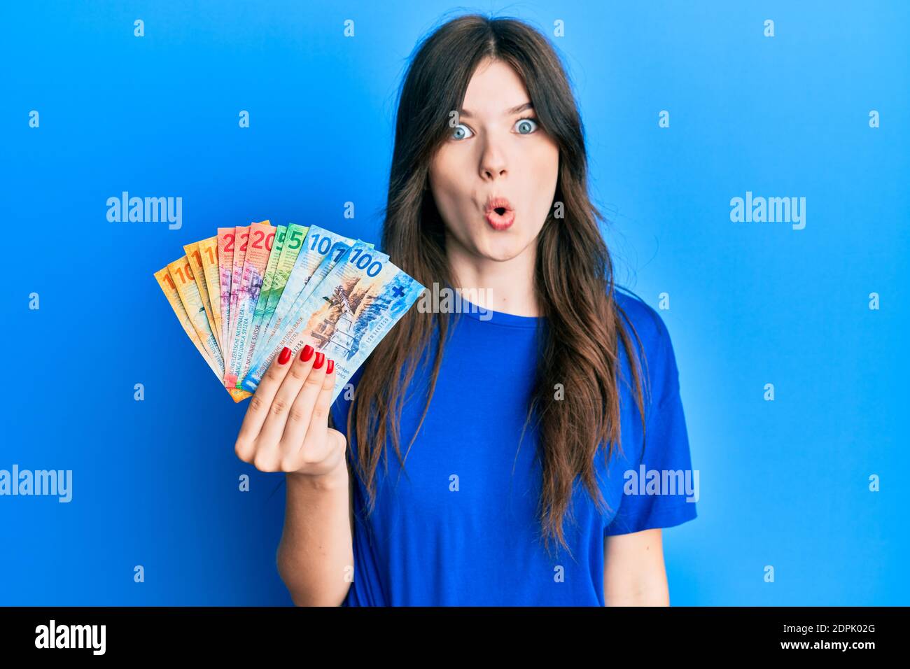 Young beautiful caucasian girl holding swiss franc banknotes scared and ...