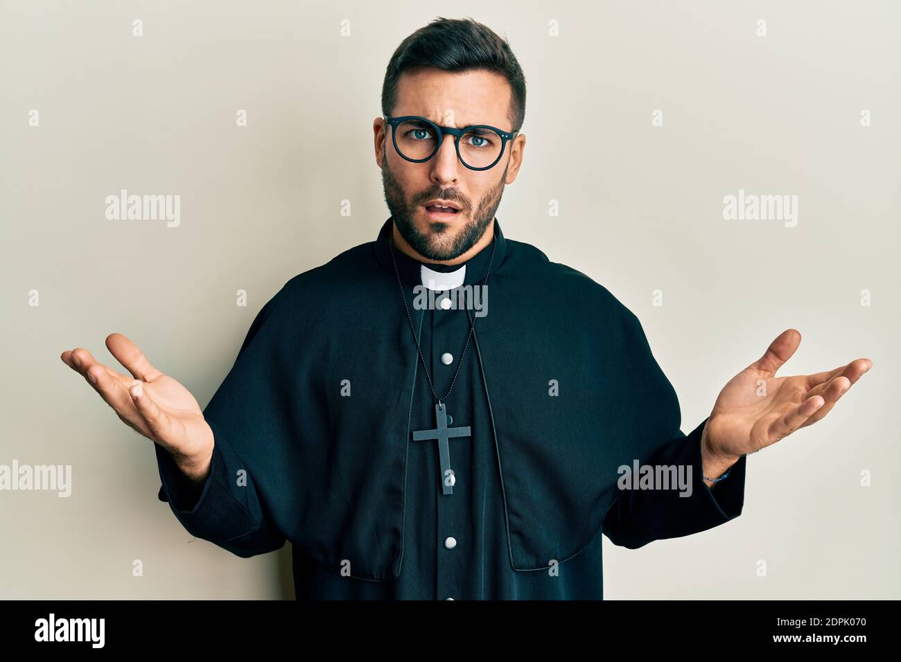 Young hispanic priest man standing over white background in shock face ...