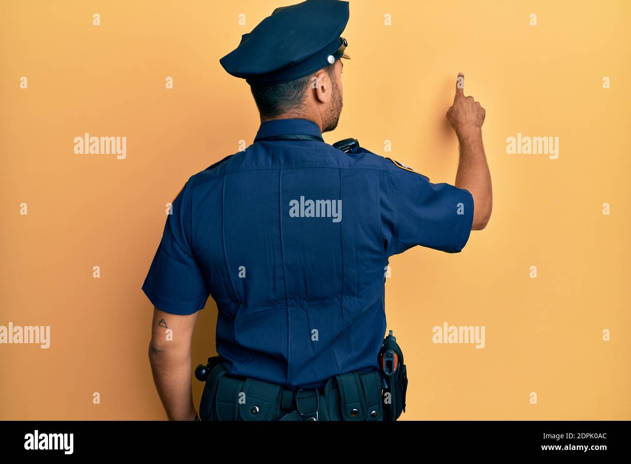 Handsome hispanic man wearing police uniform posing backwards pointing ...