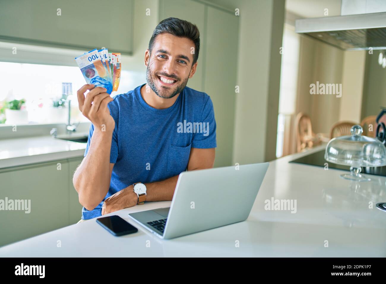 Young handsome man smiling happy holding swiss franc banknotes at home ...