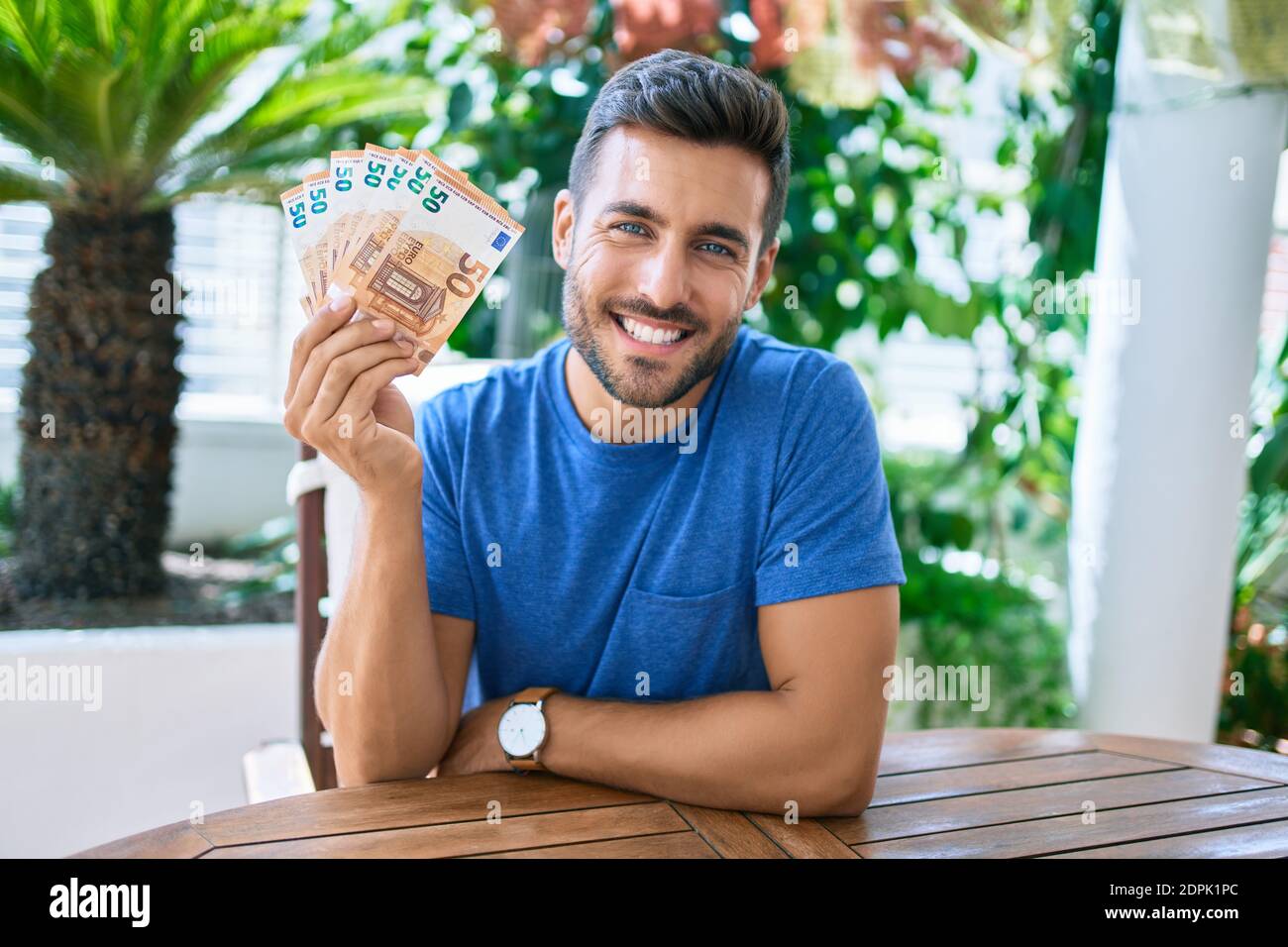 Young hispanic man smiling happy holding euros banknotes at the terrace ...