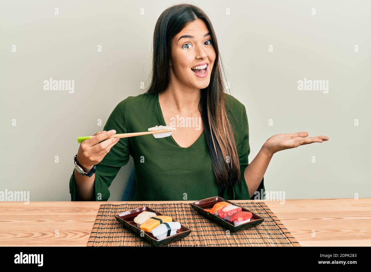Young brunette woman eating sushi sitting on the table celebrating ...