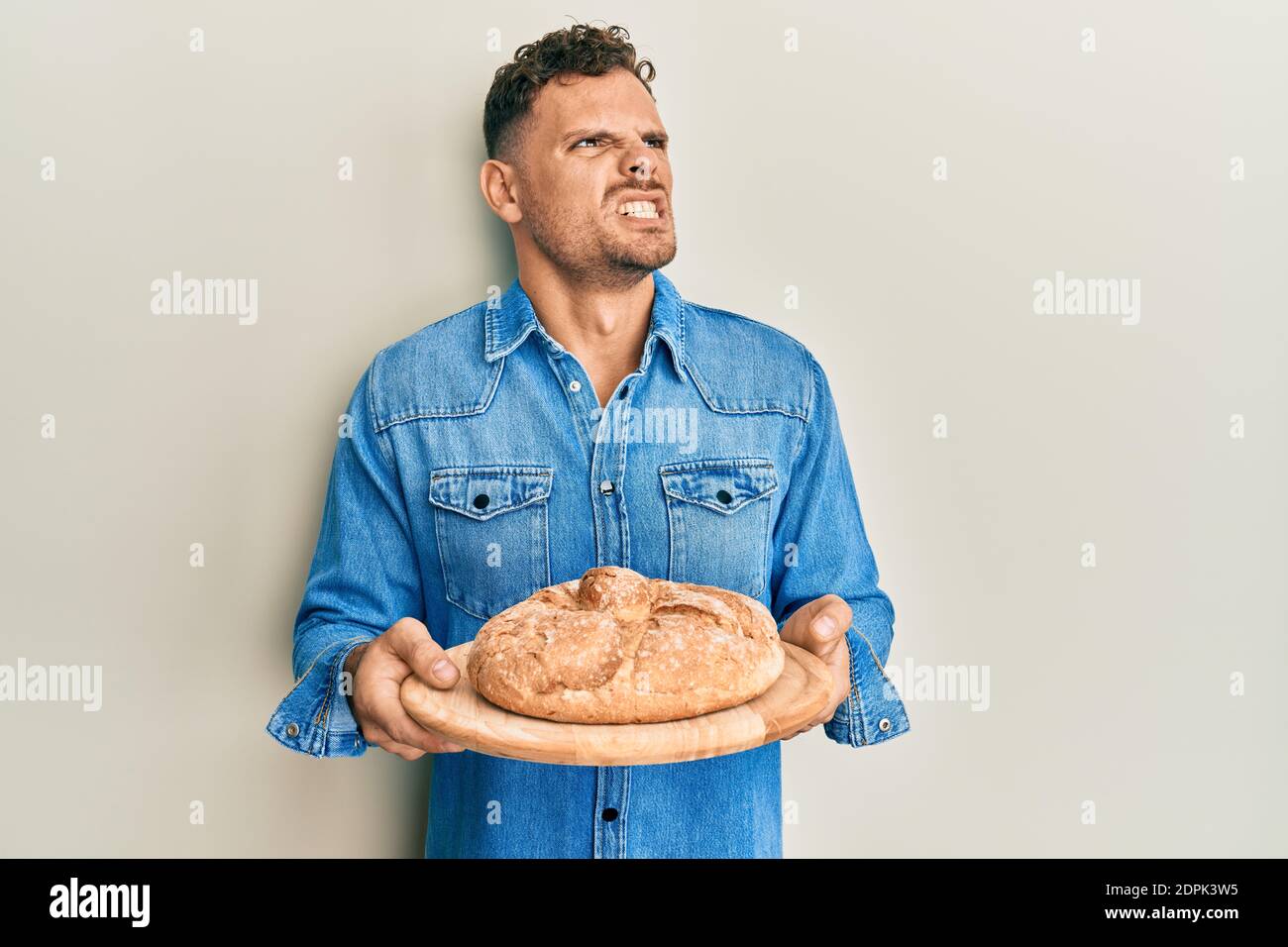 Young hispanic man holding bread angry and mad screaming frustrated and ...
