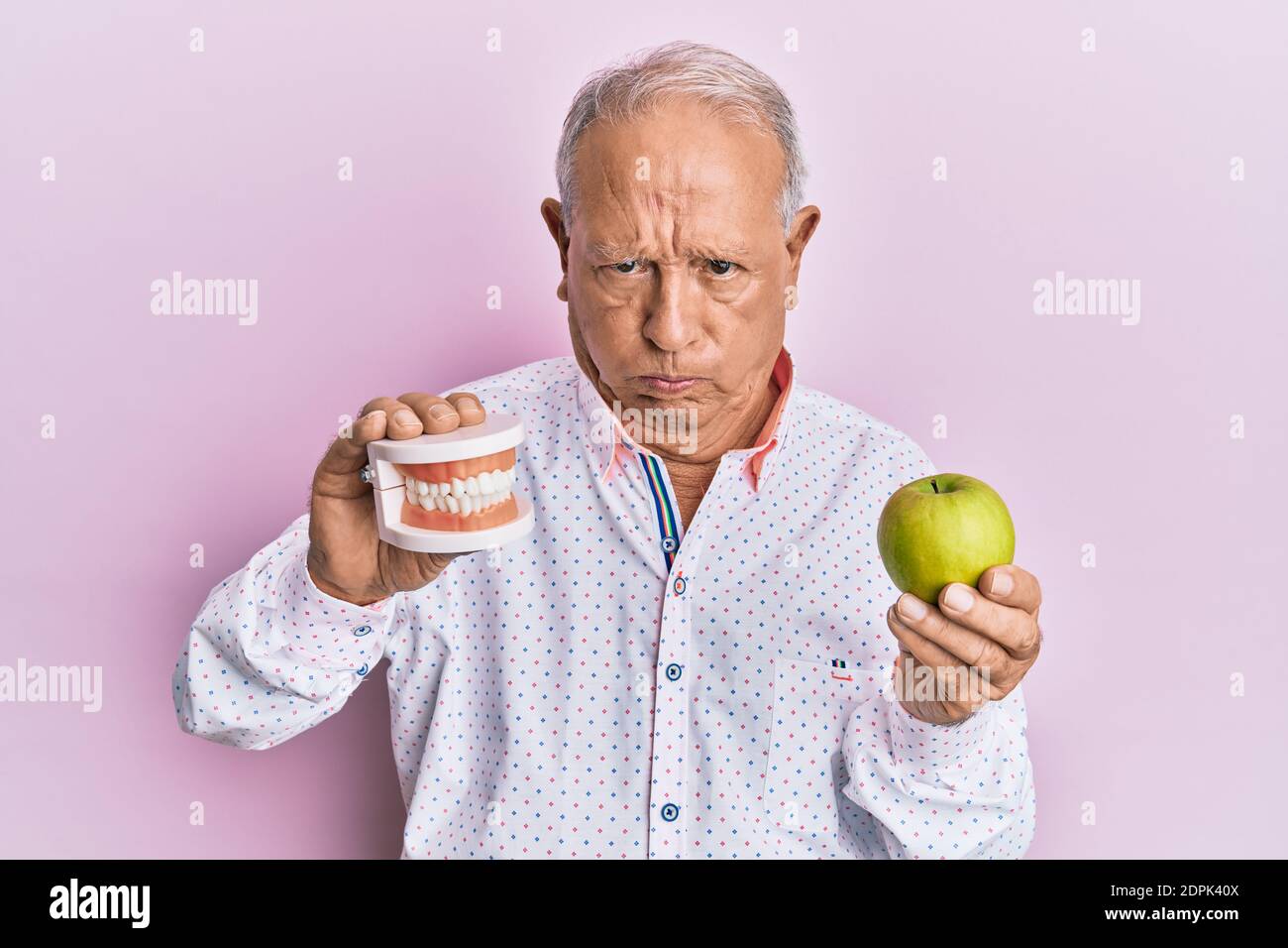 Senior caucasian man holding denture and green apple depressed and ...