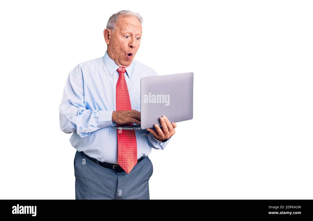 Senior handsome grey-haired man wearing tie using laptop scared and ...