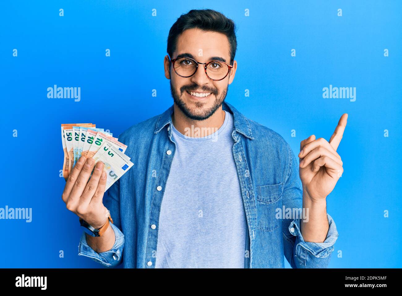 Young hispanic man holding euro banknotes smiling happy pointing with ...