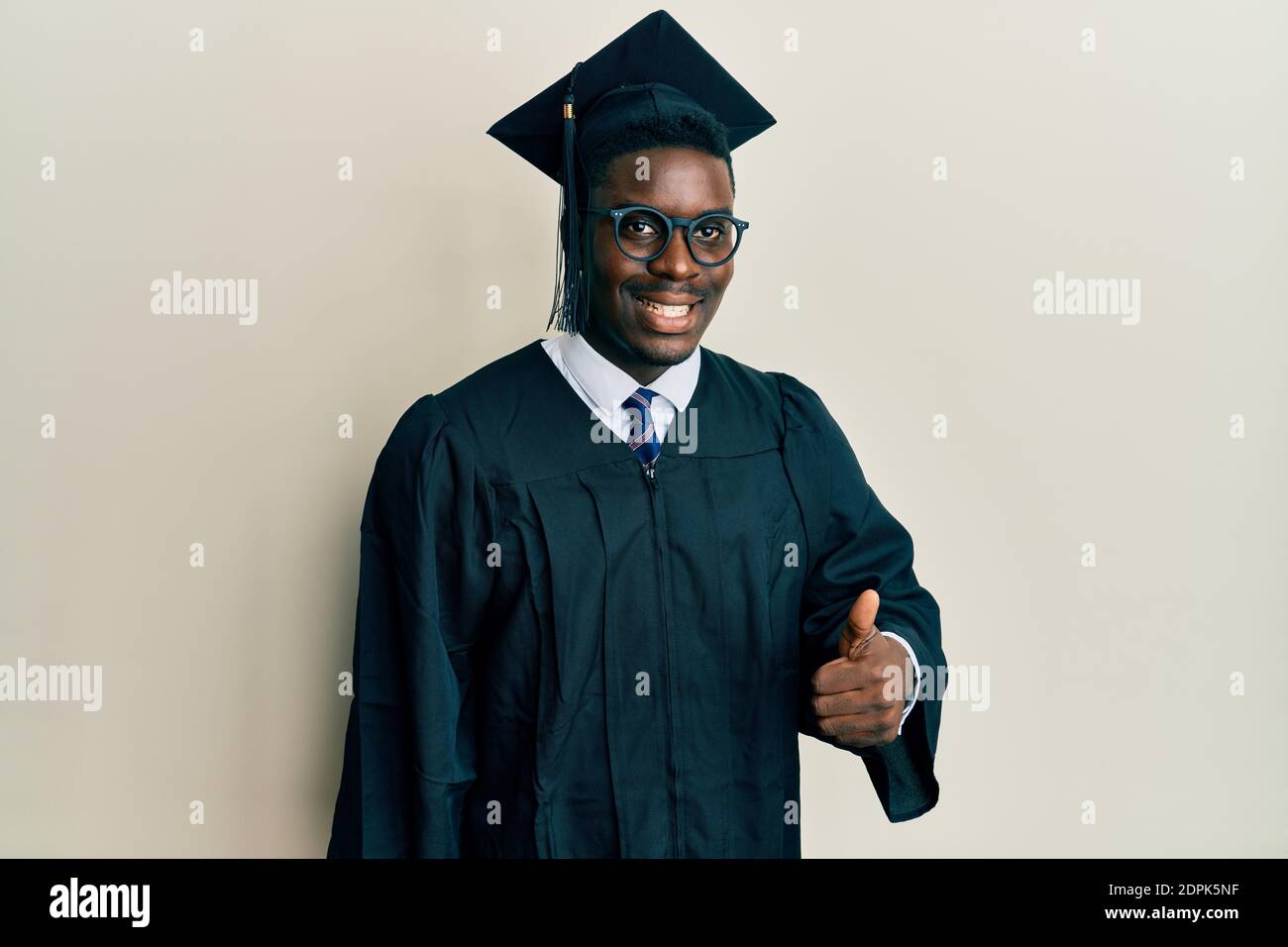 Handsome black man wearing graduation cap and ceremony robe doing happy ...