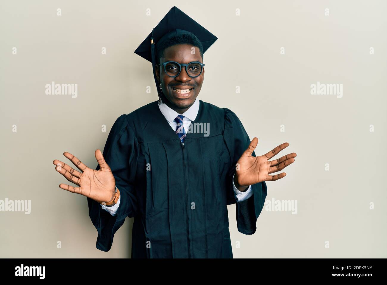 Handsome black man wearing graduation cap and ceremony robe celebrating ...