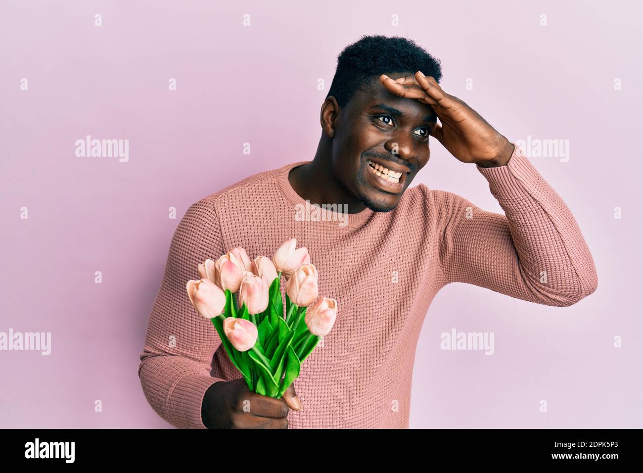Handsome black man holding bouquet of pink tulips flowers stressed and ...