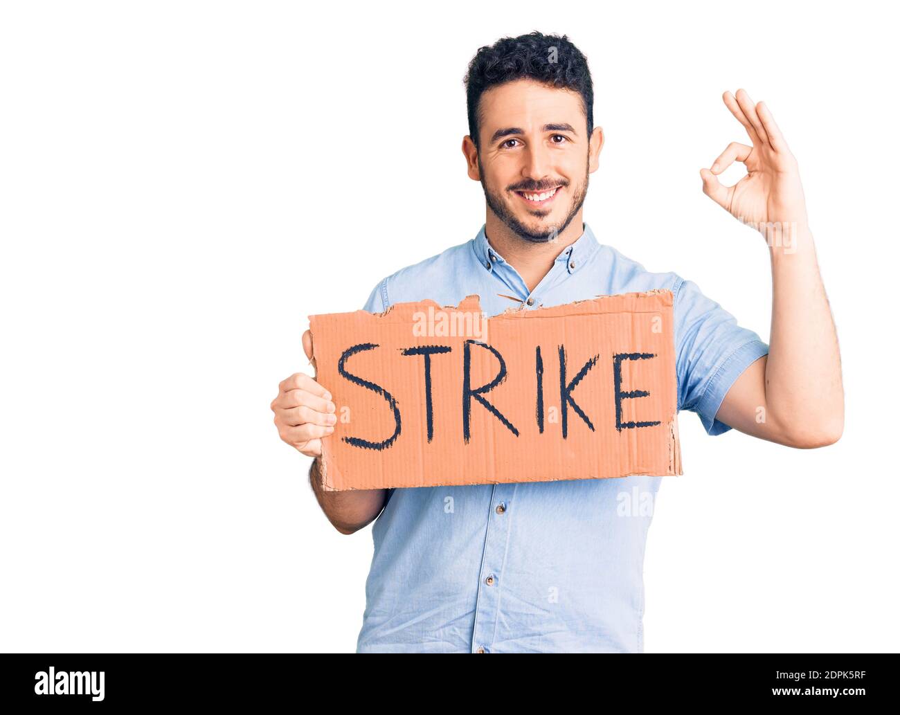 Young hispanic man holding strike banner cardboard doing ok sign with ...
