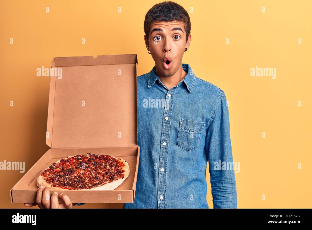 Young african amercian man holding delivery pizza box scared and amazed ...