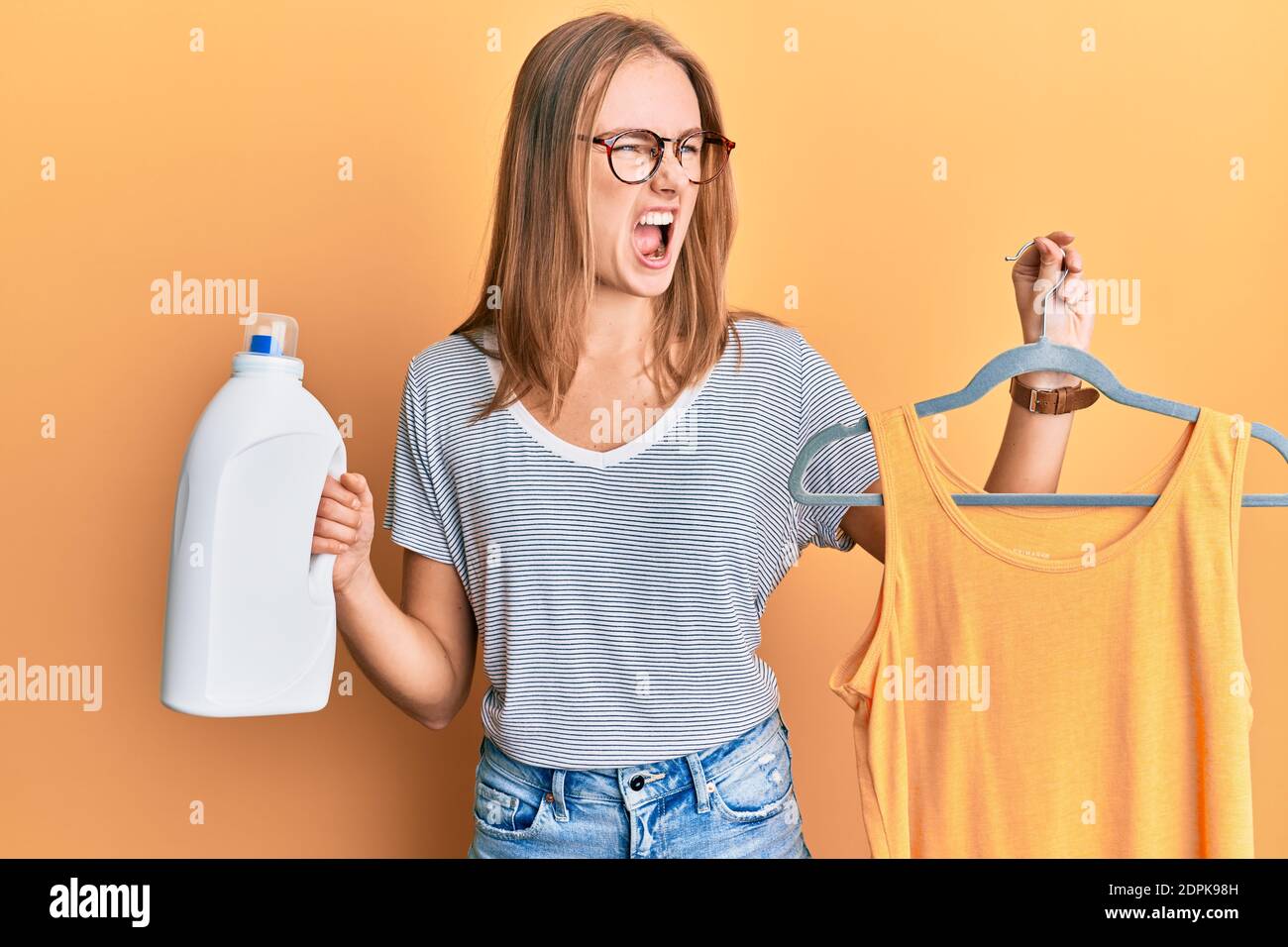 Beautiful blonde woman holding shirt on hanger and detergent bottle ...