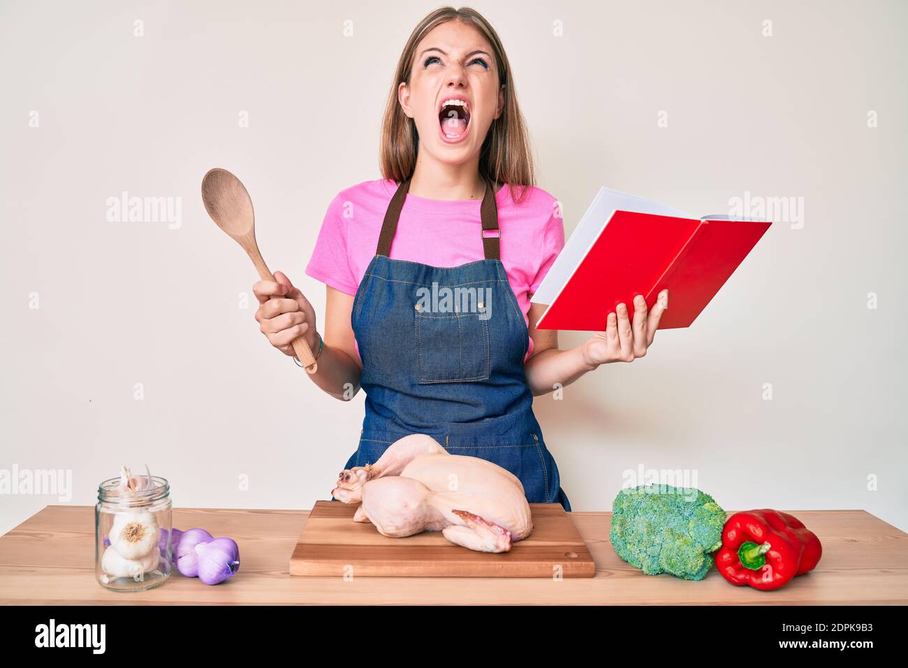Young blonde girl wearing professional baker apron reading cooking ...