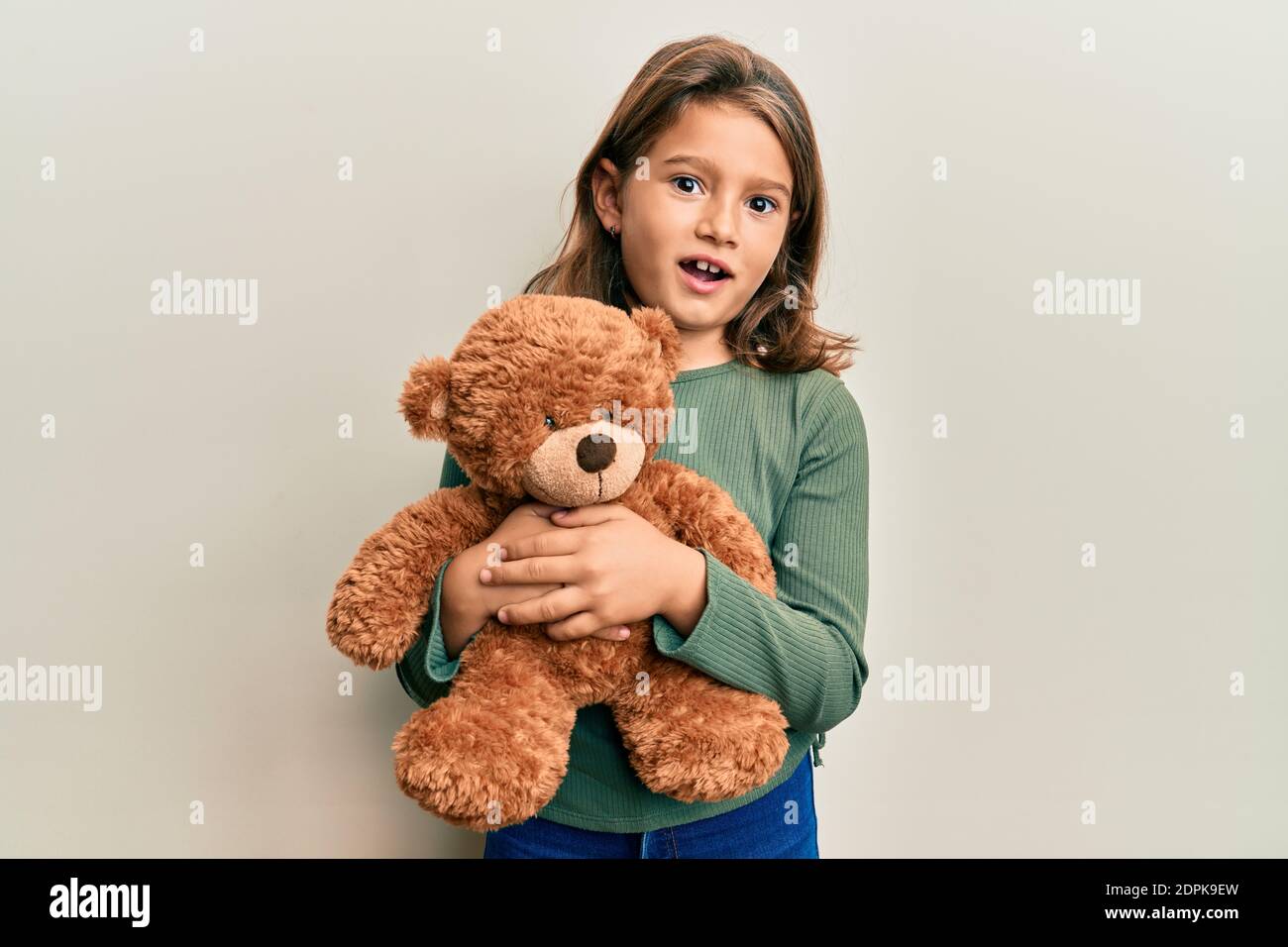 Little beautiful girl hugging teddy bear in shock face, looking ...