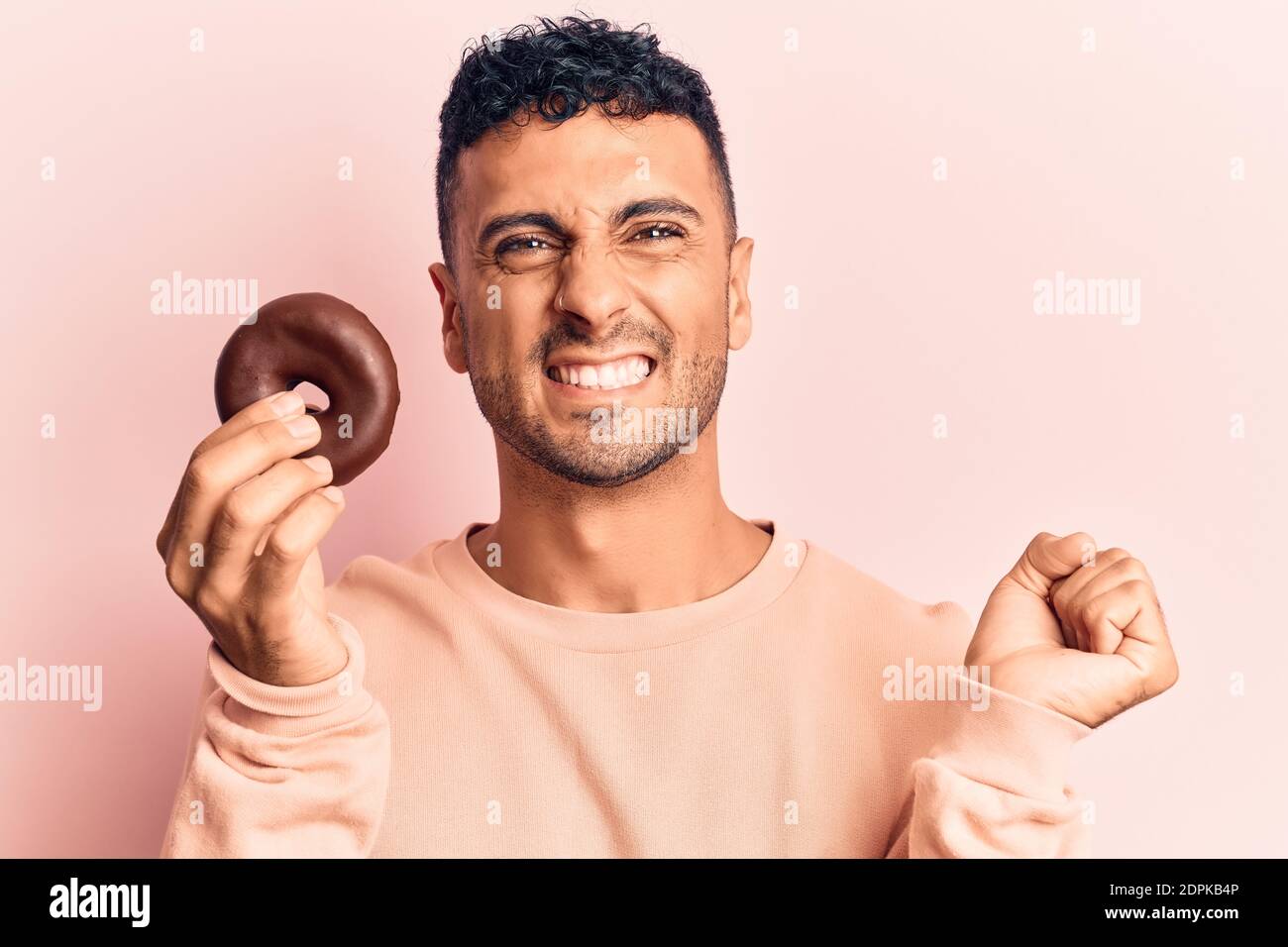 Young hispanic man holding donut screaming proud, celebrating victory ...
