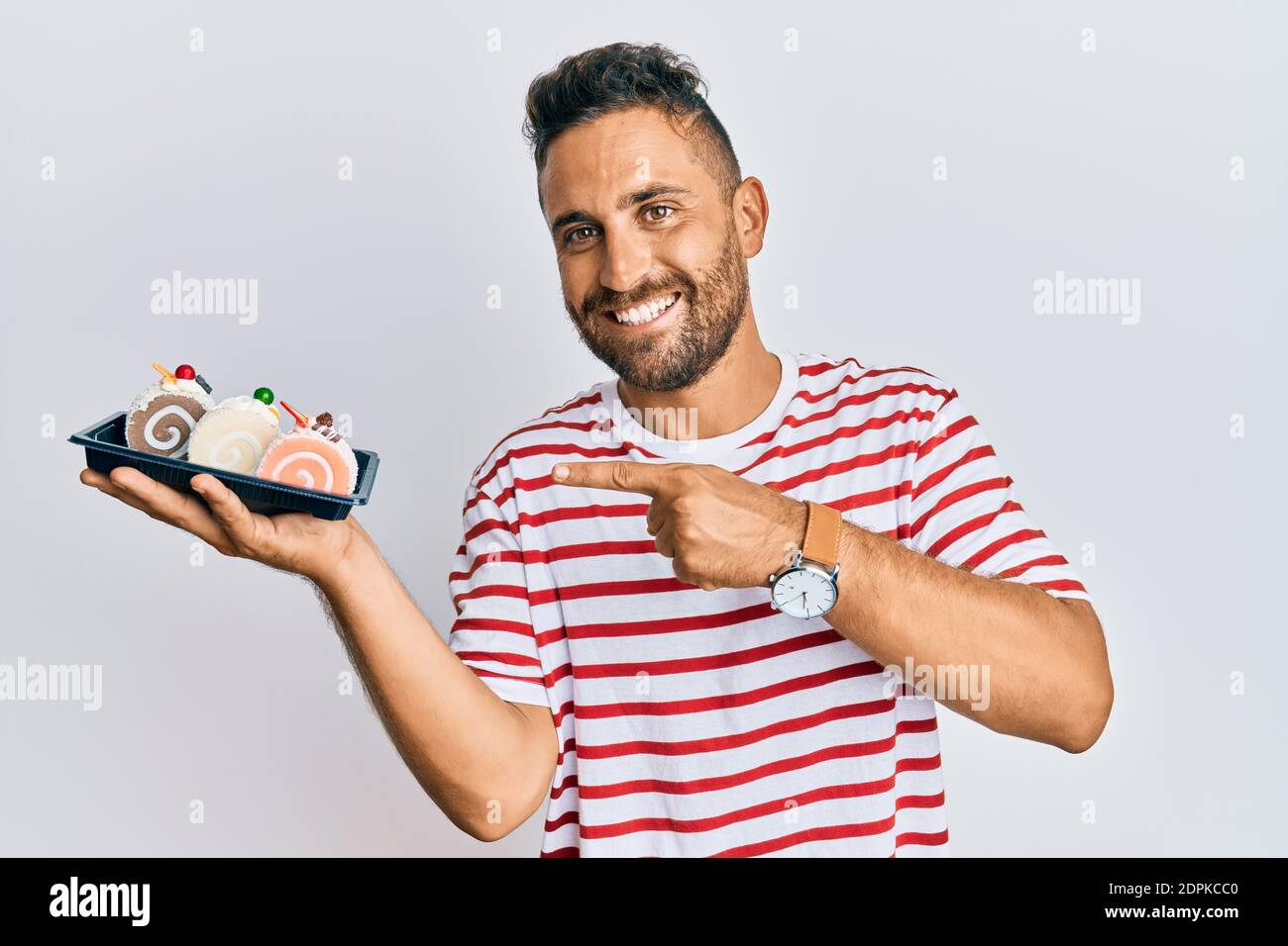 Handsome man with beard holding cake sweets smiling happy pointing with ...