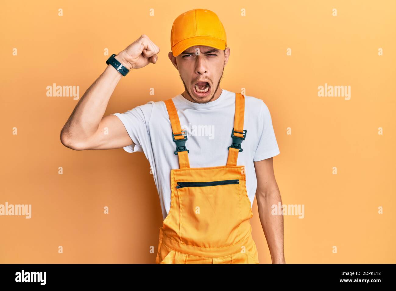 Hispanic young man wearing handyman uniform angry and mad raising fist ...
