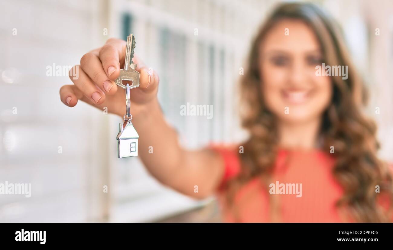 Young blonde girl smiling happy holding key of new house standing at ...