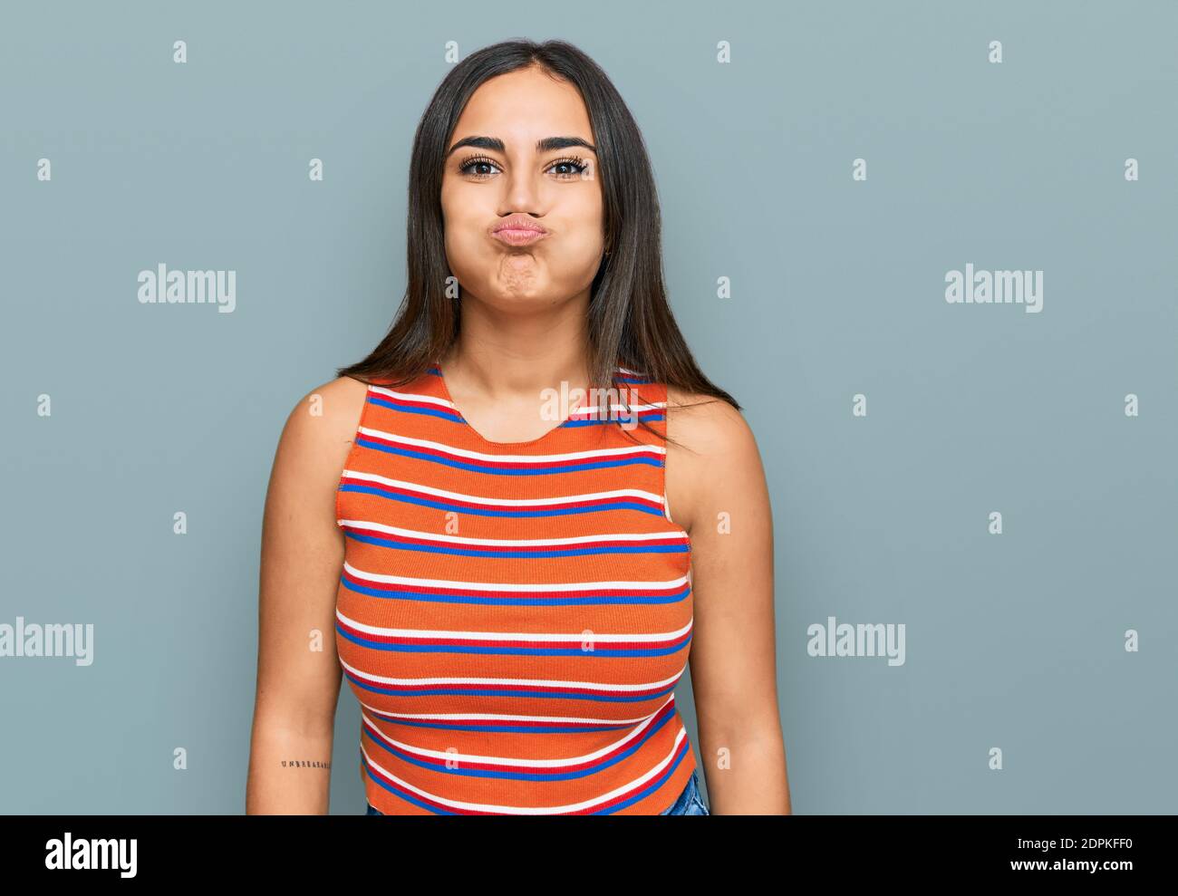 Young brunette woman wearing casual clothes puffing cheeks with funny ...